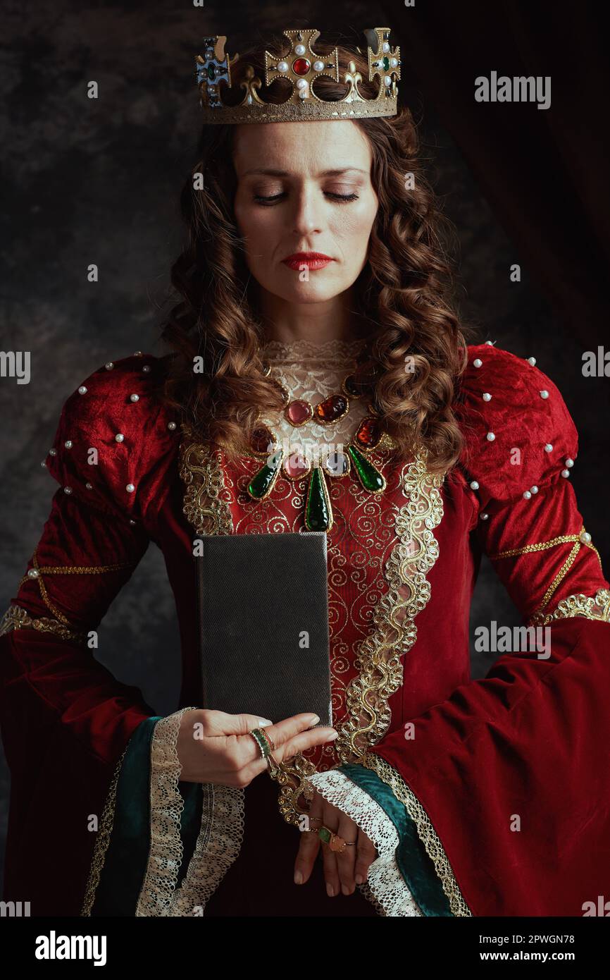medieval queen in red dress with book and crown on dark gray background ...