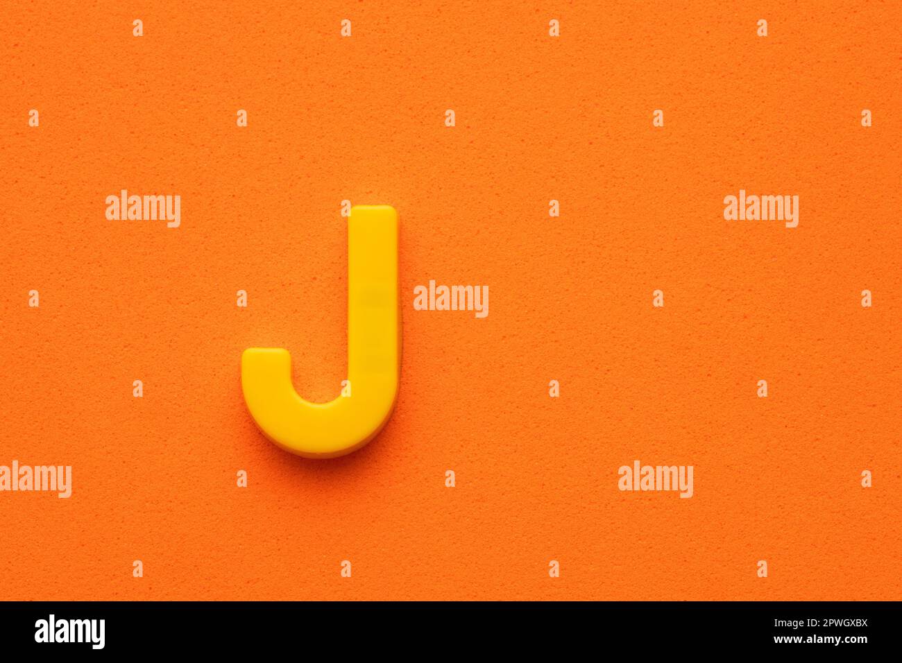Alphabet letter J - Yellow plastic piece on orange foamy background ...