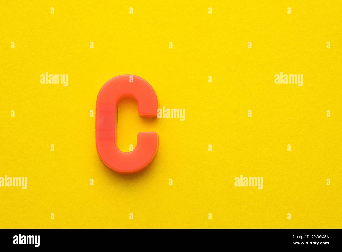 Peach colored plastic letter C uppercase on yellow foamy background ...
