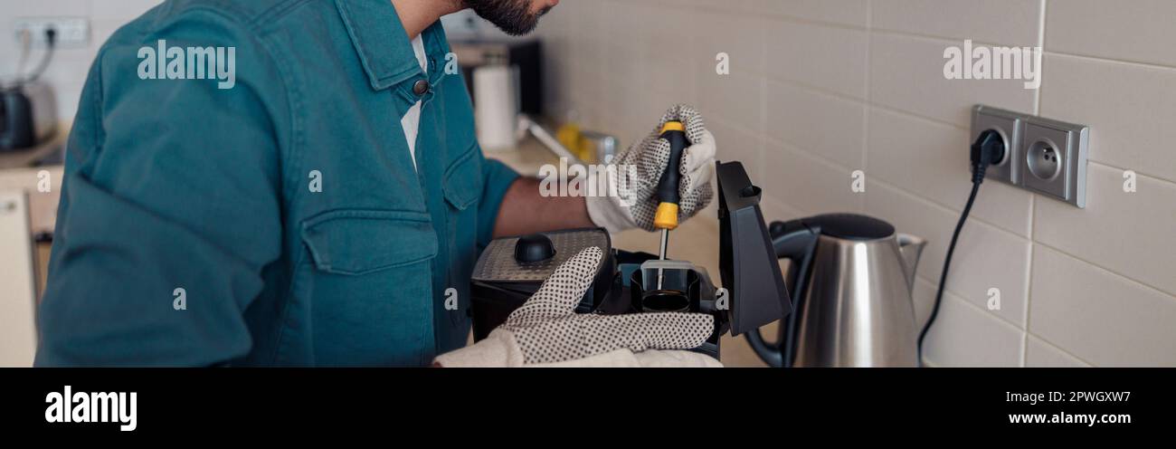Man with screwdriver fixing coffee machine at table in kitchen ...