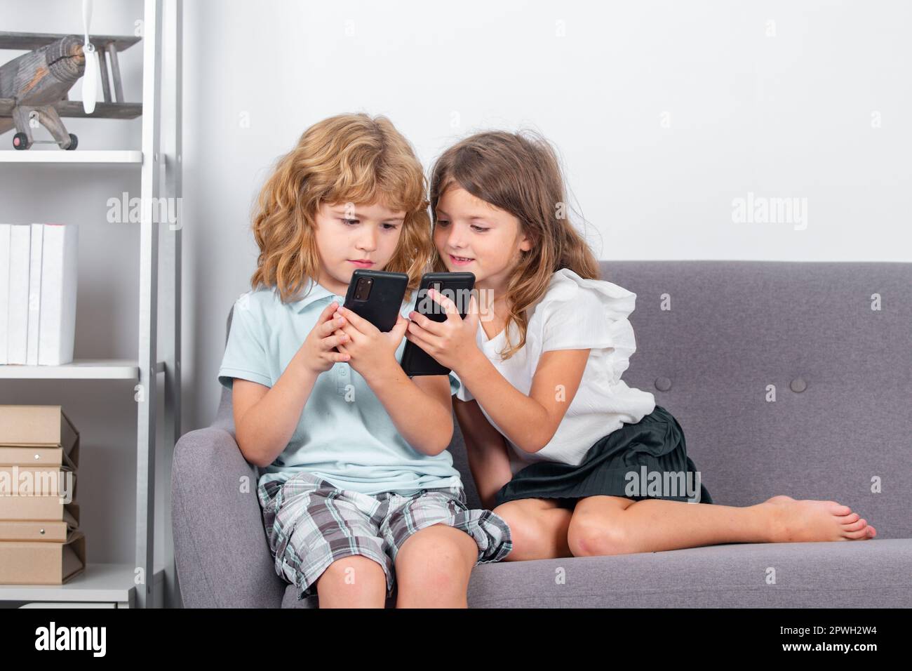 Kids playing smartphone. Brother and sister at home playing video games ...