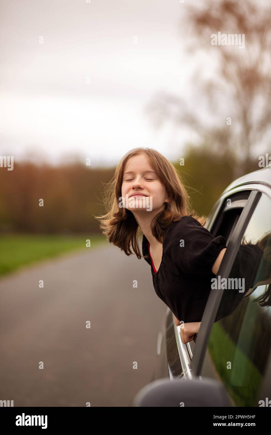 happy girl looks out of the car window closing her eyes on a summer day ...
