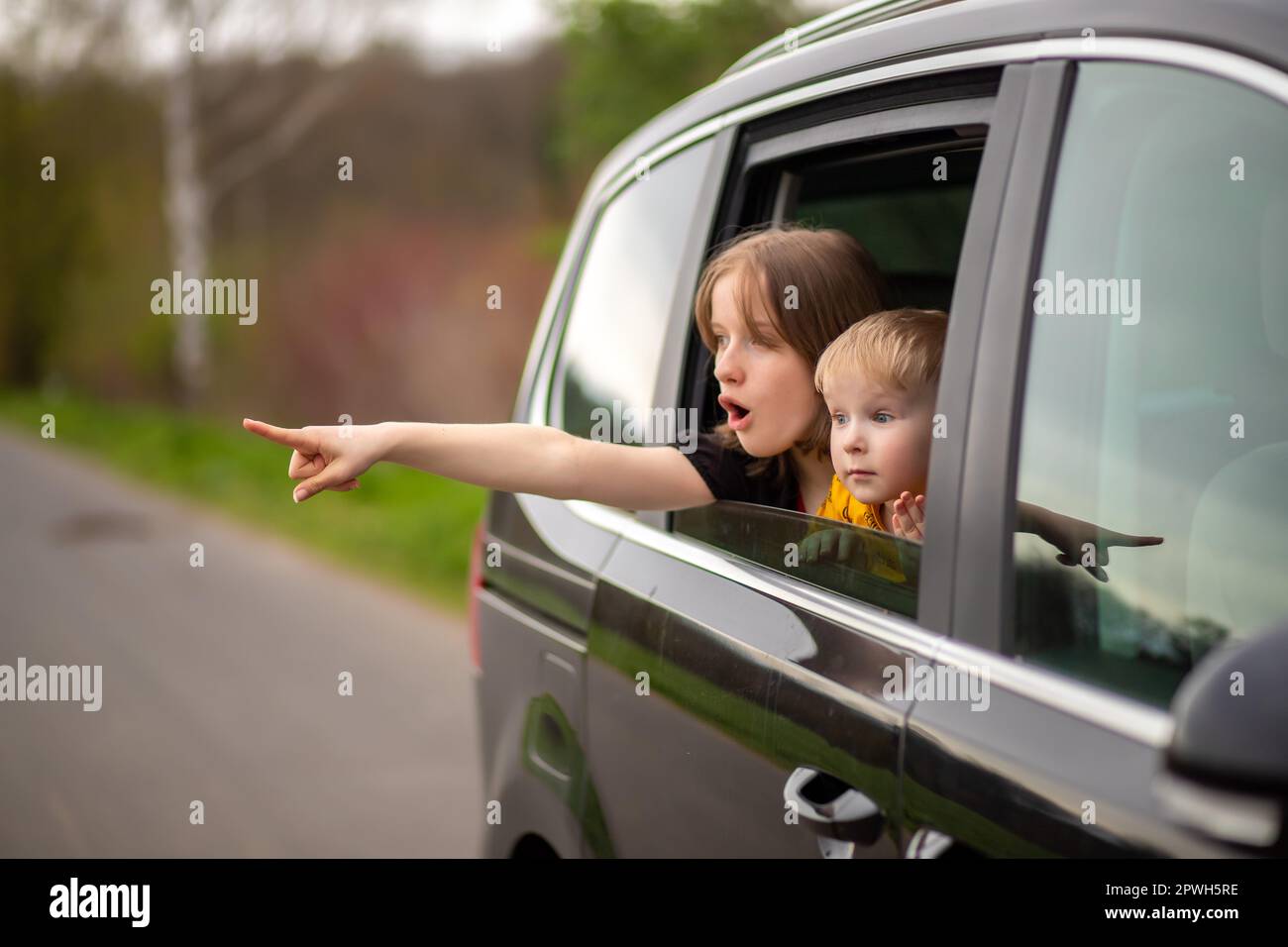 Happy brother and sister looking out car window , point the finger to ...
