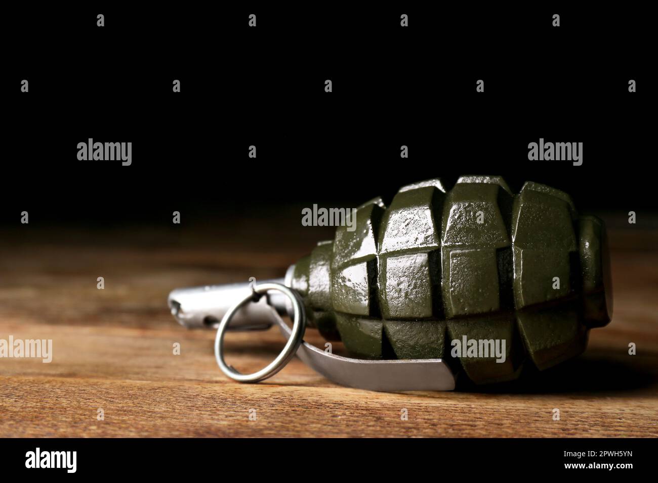 Hand grenade on wooden table against black background, closeup. Space ...