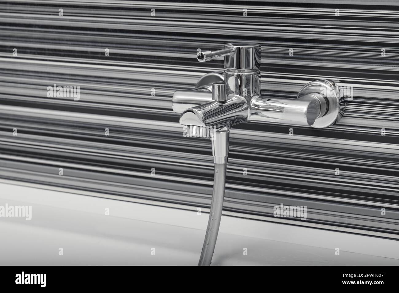 Shiny water tap installed on black and white wall above bathtub Stock ...