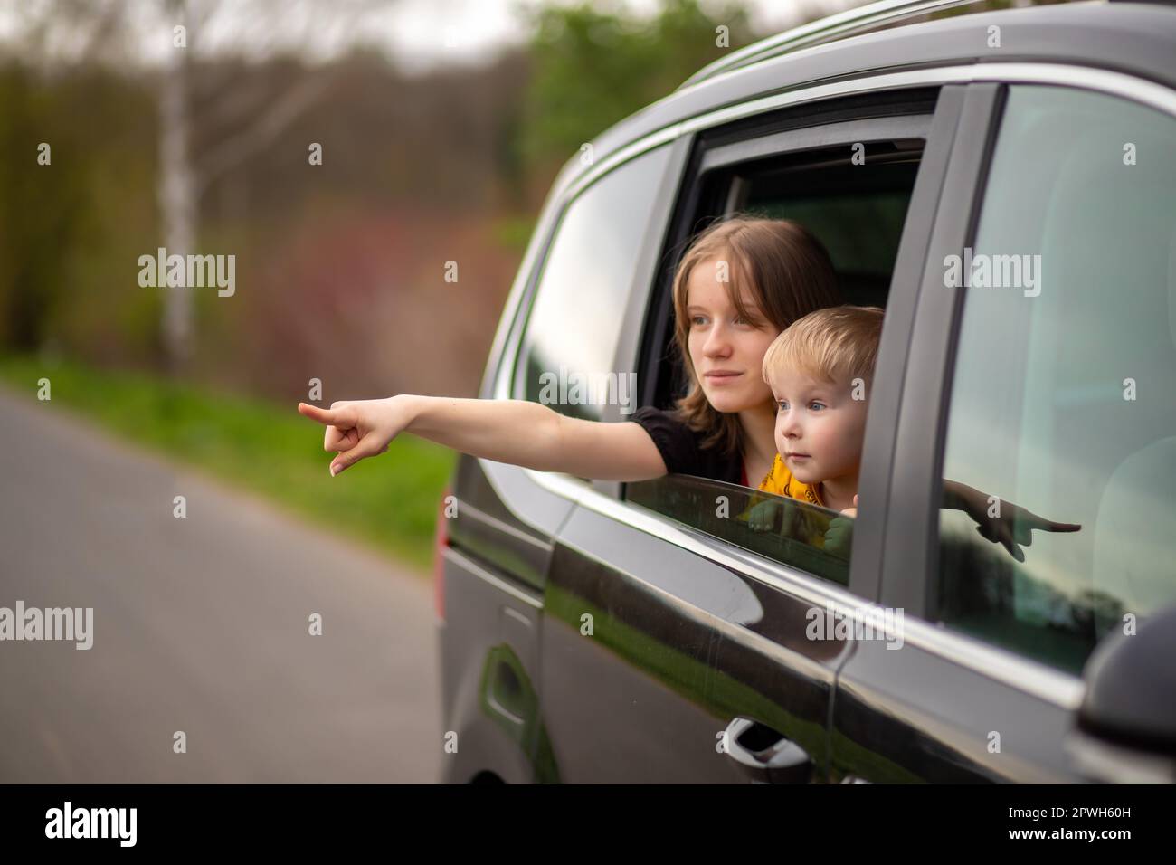 Happy brother and sister looking out car window , point the finger to ...