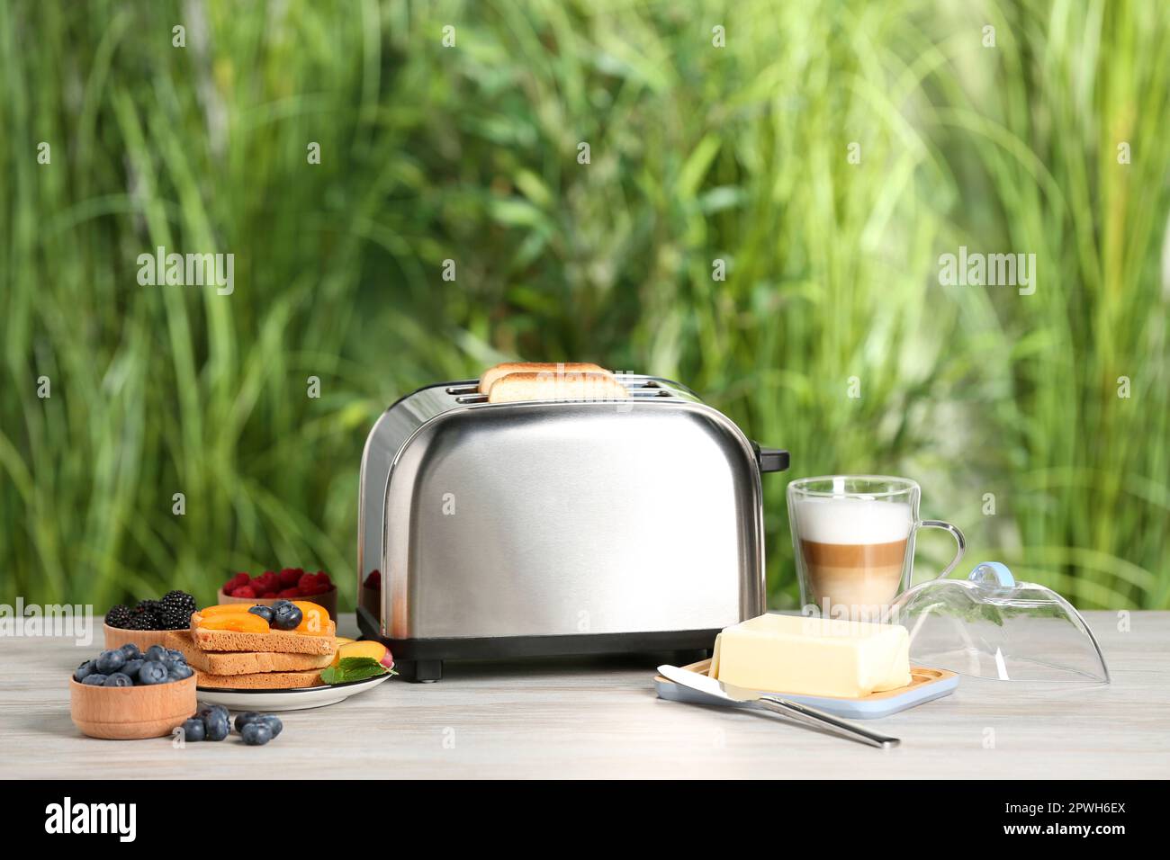 Modern toaster and fresh products on white wooden table against blurred ...