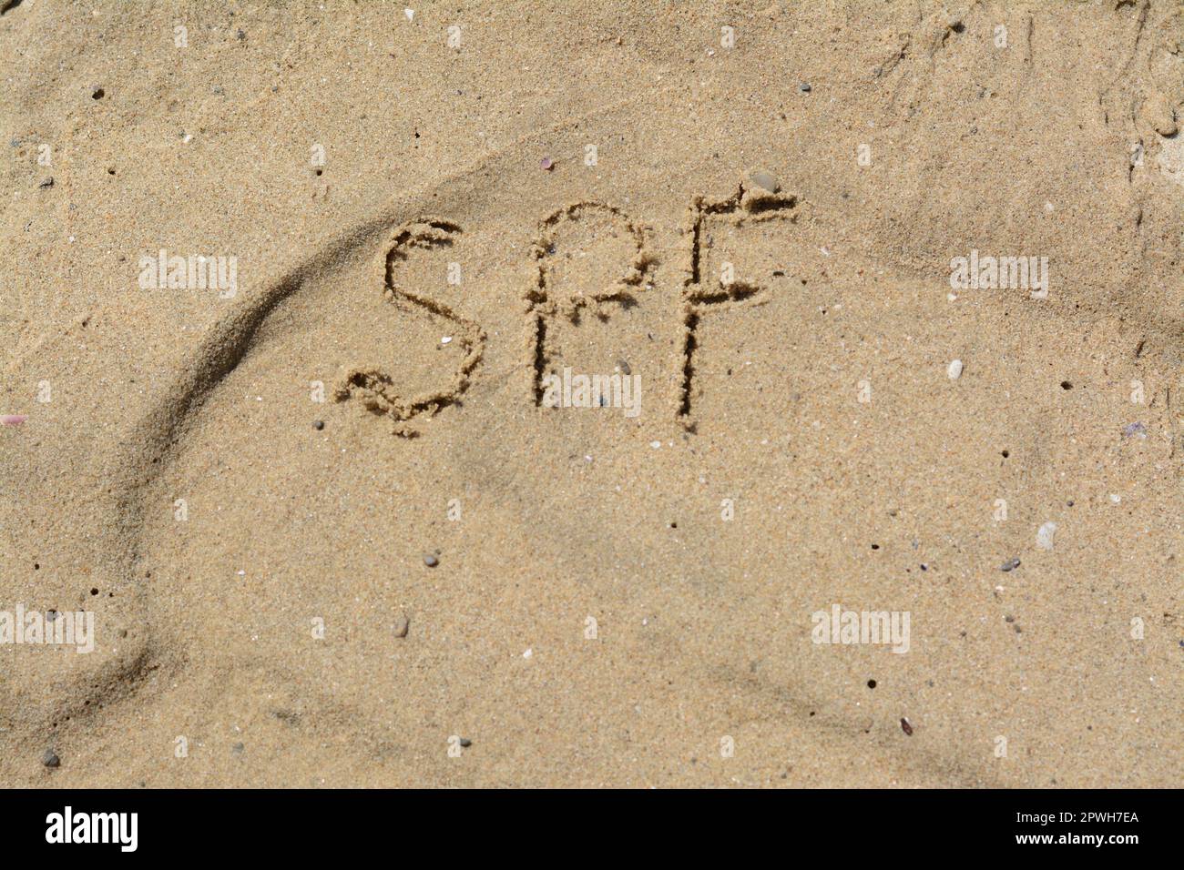 Abbreviation SPF written on sand at beach, top view. Space for text ...