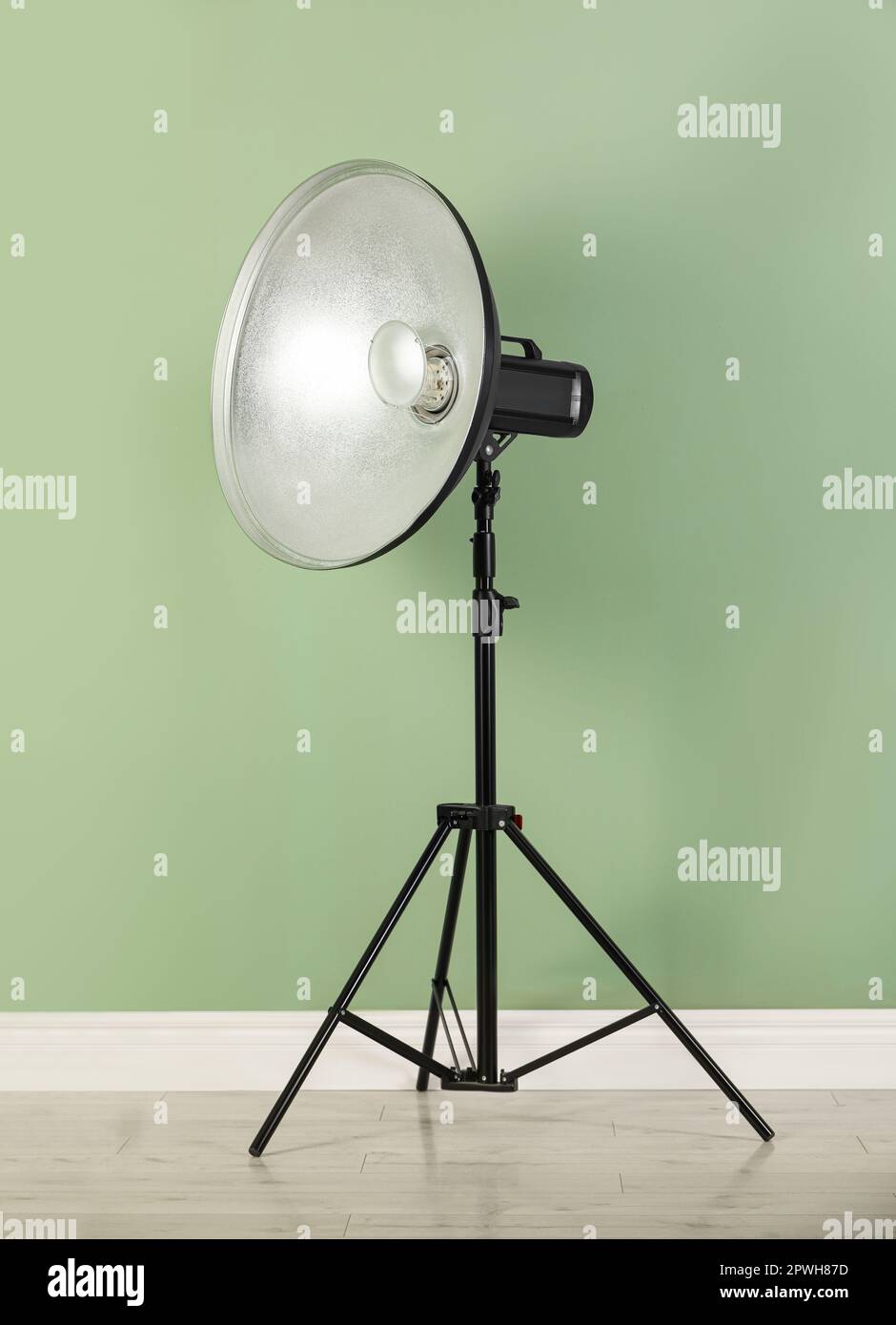 Professional beauty dish reflector on tripod near pale green wall in ...