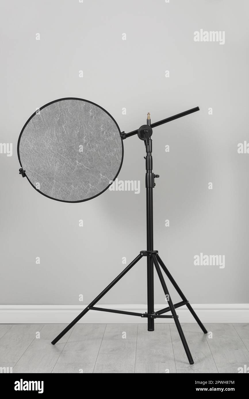 Studio reflector on tripod near grey wall indoors. Professional ...