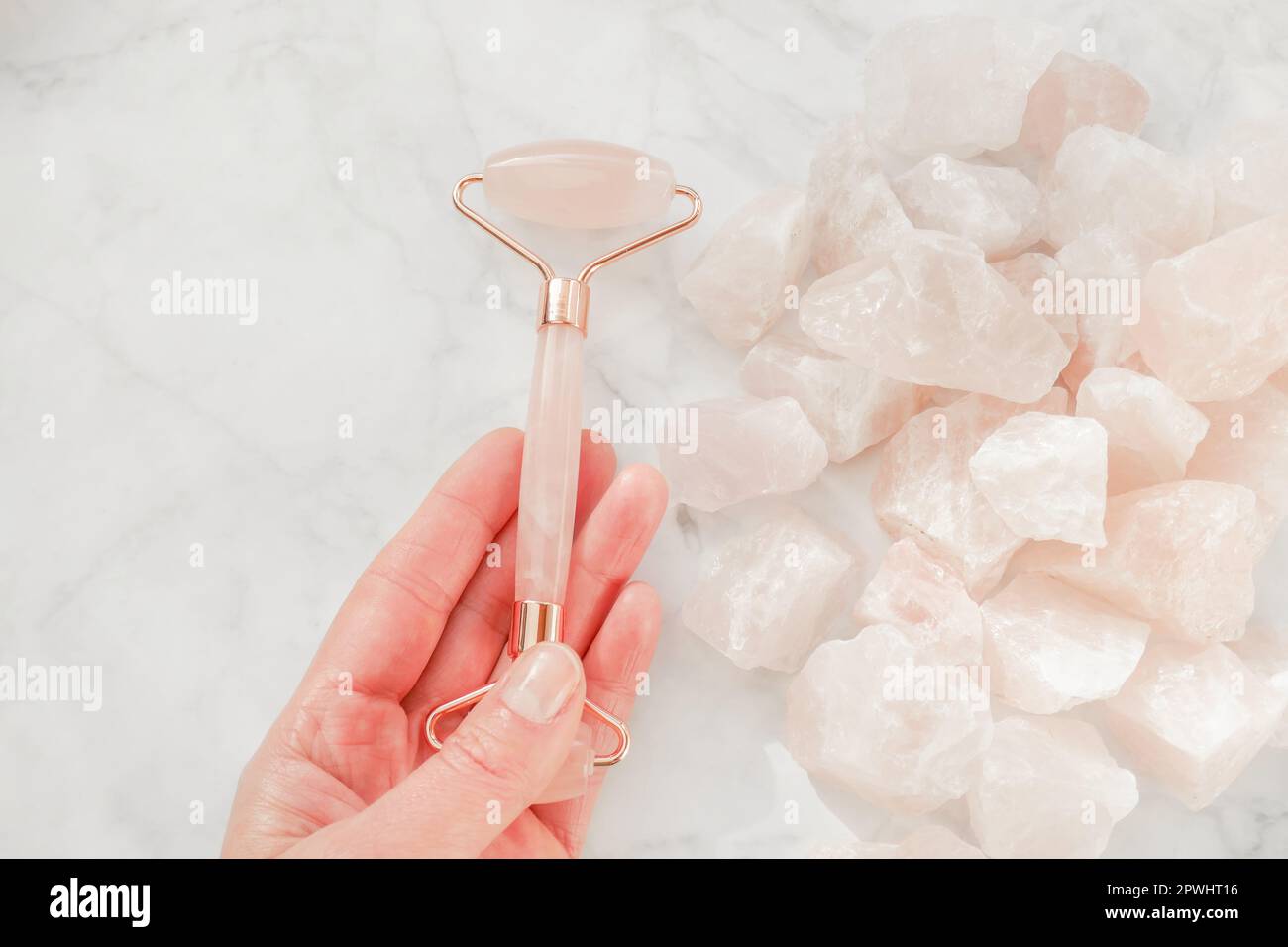 Rose quartz Massage roller in a womans hand on rose quartz on gray ...