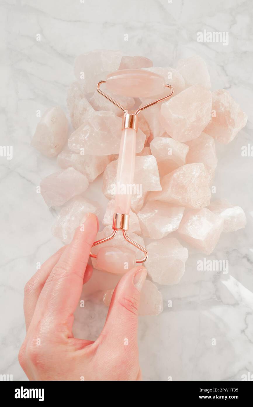 Rose quartz roller in a womans hand on rose quartz on gray marble ...