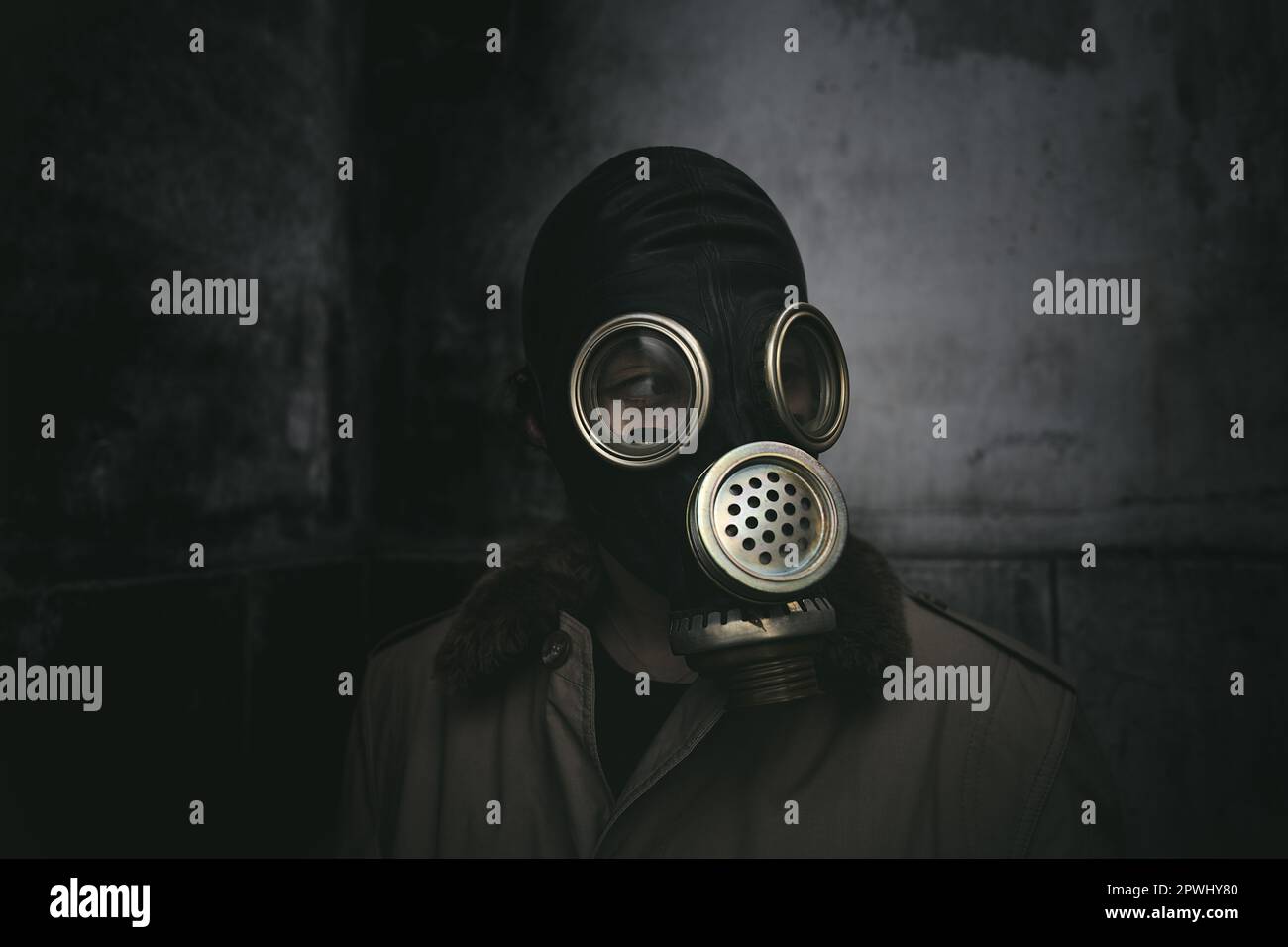 A man wearing a gas mask staying in the dark in a dilapidated building ...