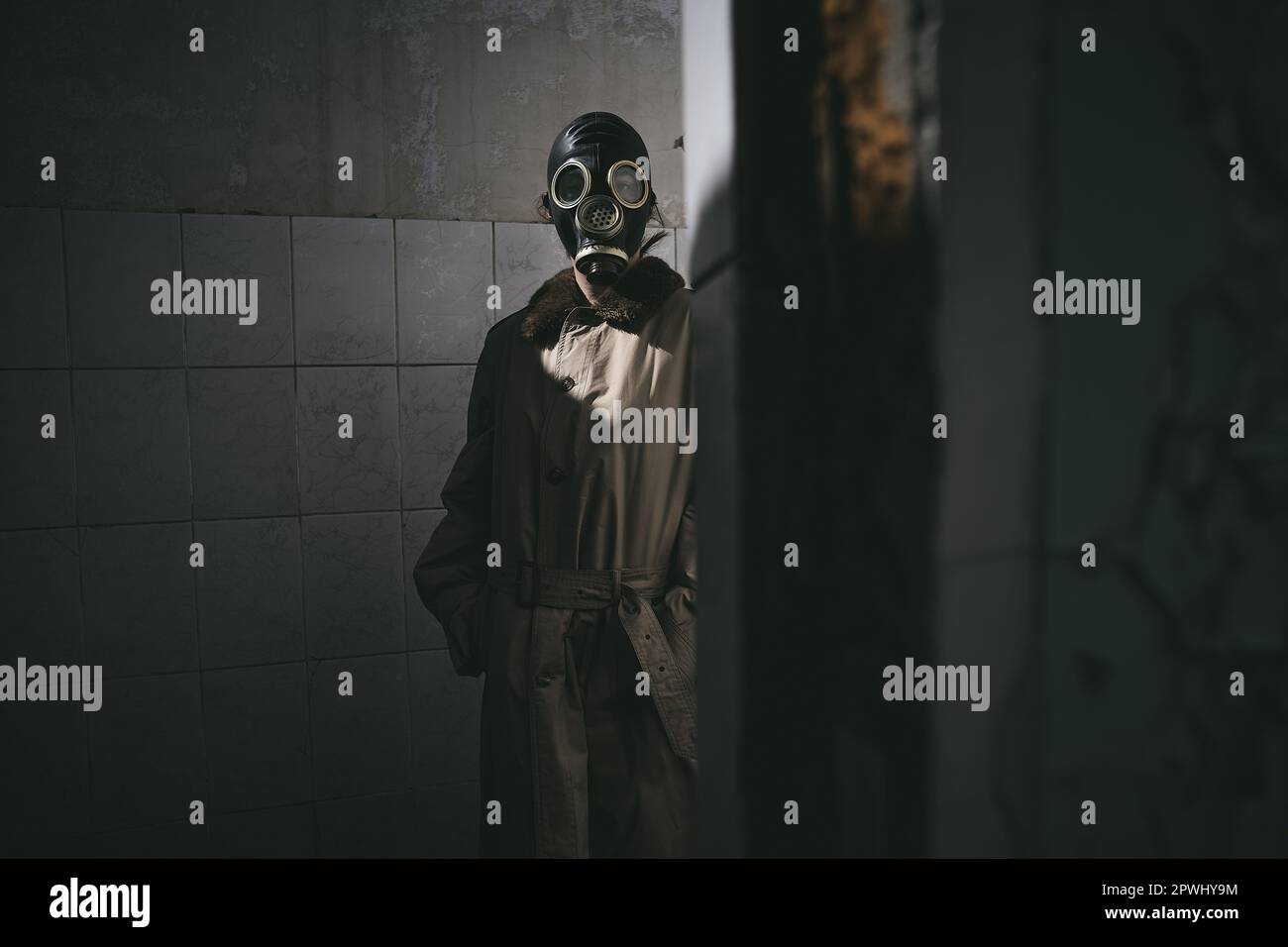 A man in gas mask standing inside an old building, peeking around the ...