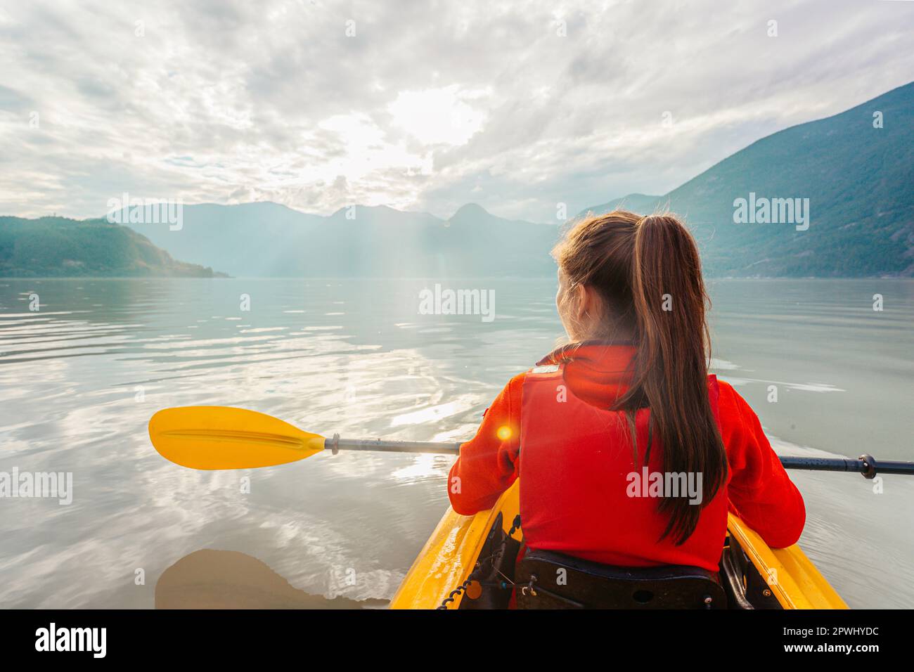 Woman kayaking paddling in kayak in fjord surrounded by mountains ...
