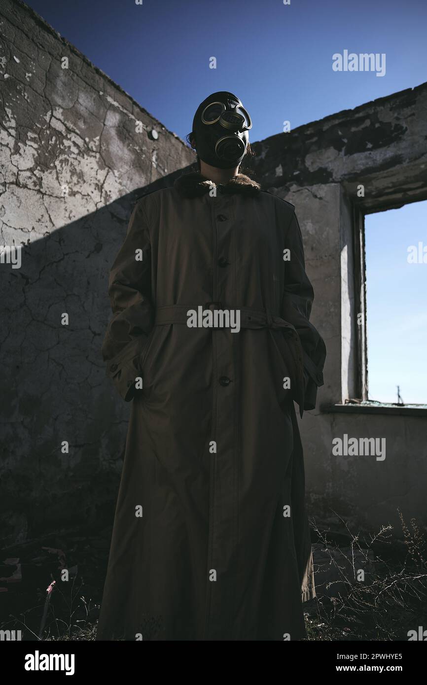 a person standing in front of a wall wearing a gas mask and trench coat ...