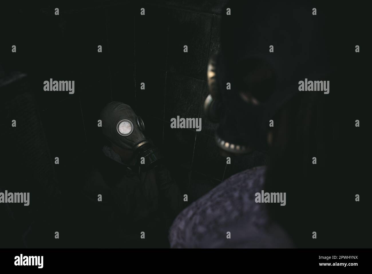 A girl in a gas mask is viewed from the back, standing and looking down ...