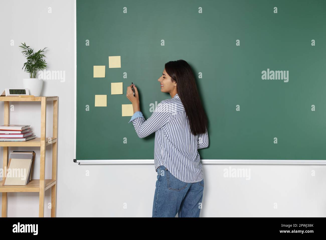 Happy young teacher giving lesson at blackboard in classroom. Space for ...