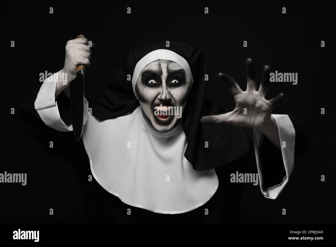 Scary devilish nun with knife on black background. Halloween party look ...