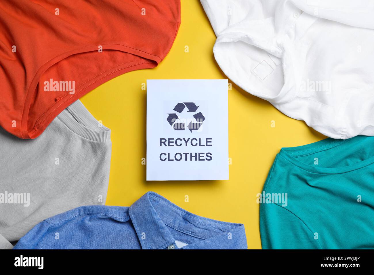 Different clothes with recycling label on yellow background, flat lay ...