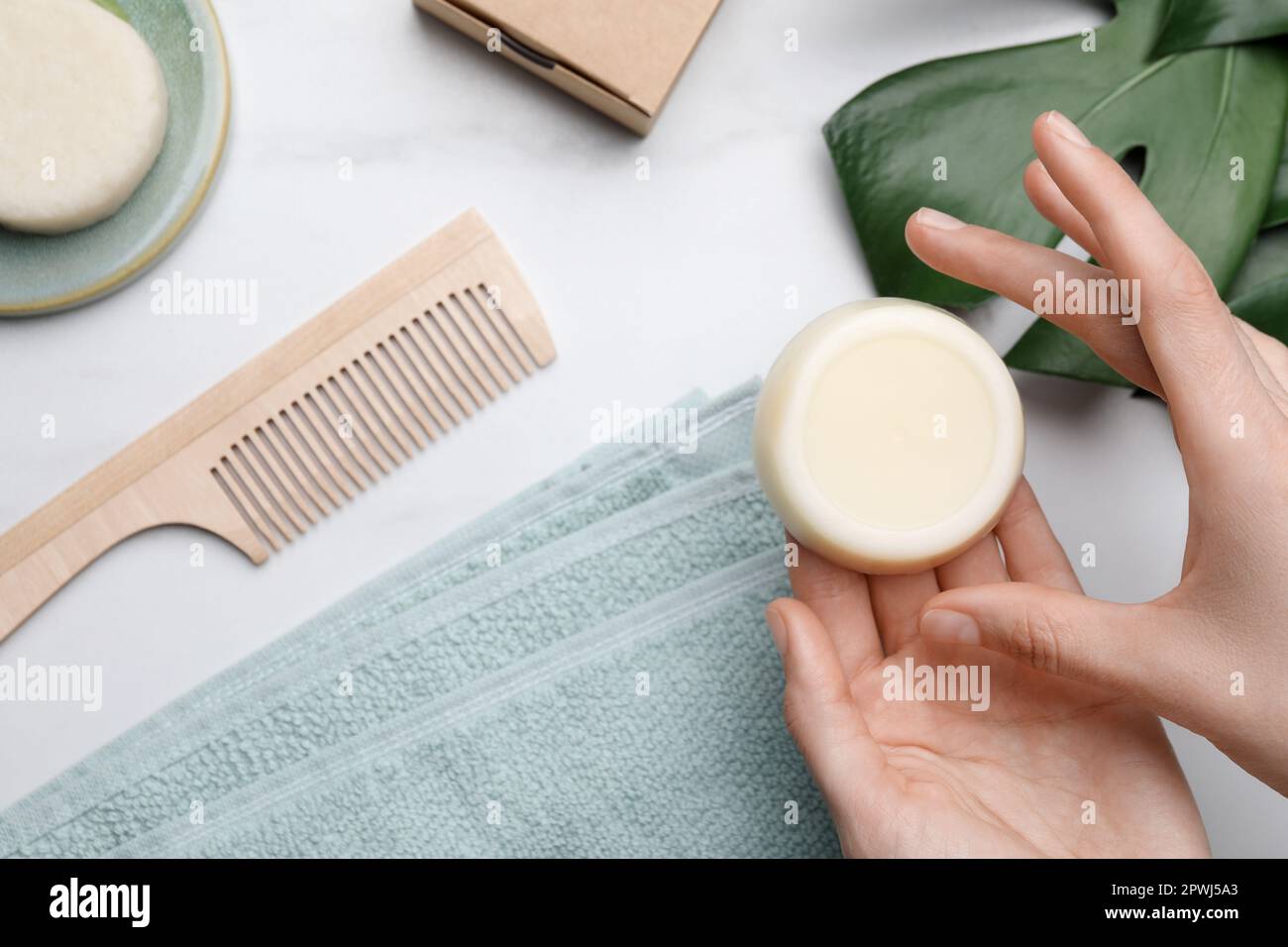 Woman holding solid shampoo bar at marble table, top view. Hair care ...