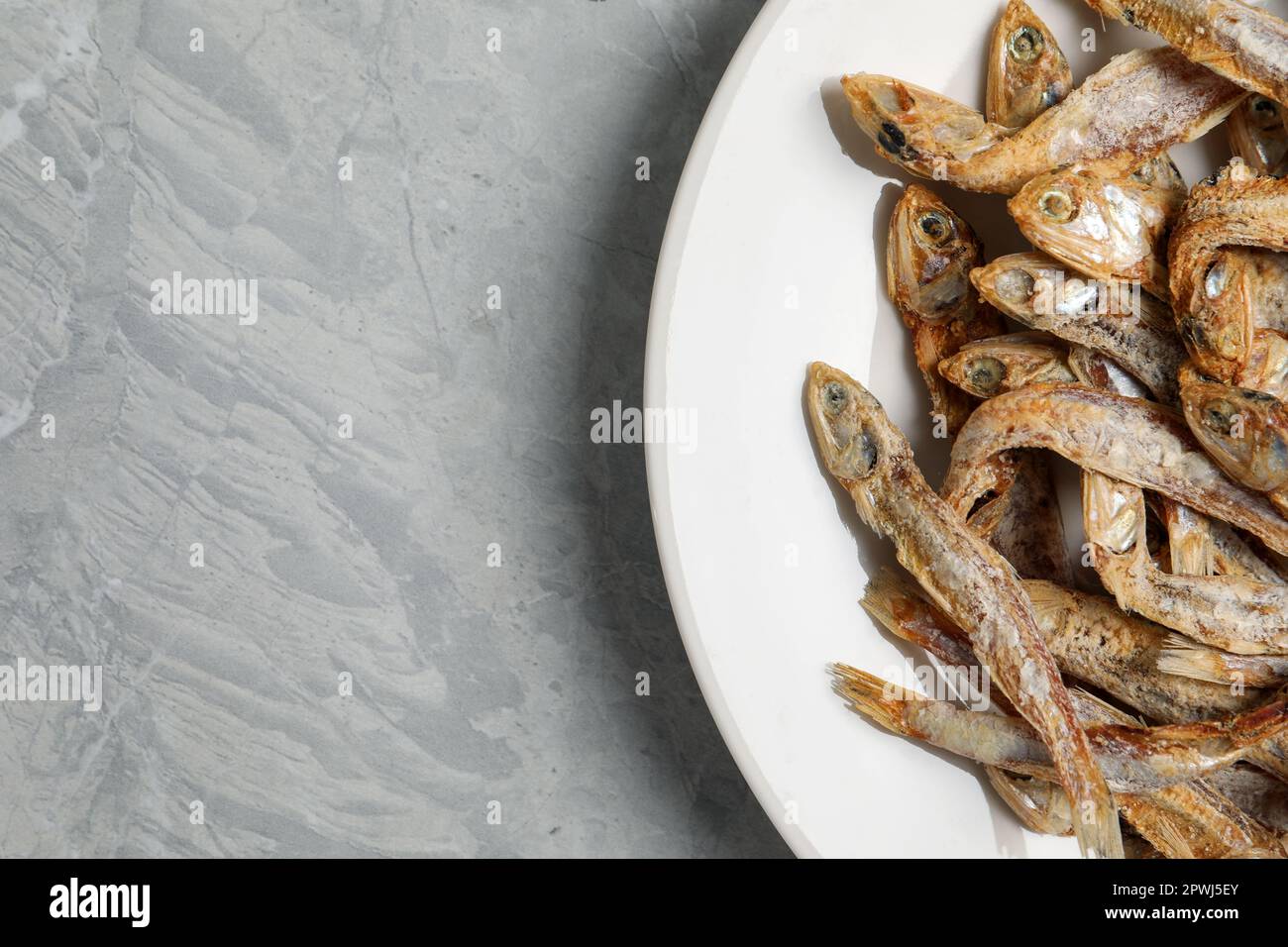 Plate of tasty dried anchovies on light grey marble table, top view ...