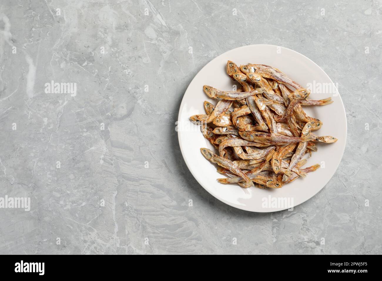 Plate of tasty dried anchovies on light grey marble table, top view ...