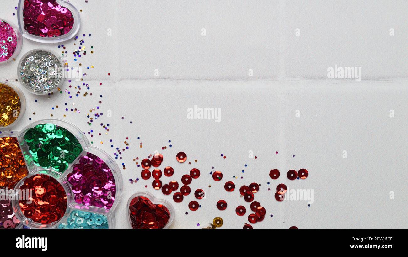 Many different colorful sequins in containers on white tiled background ...