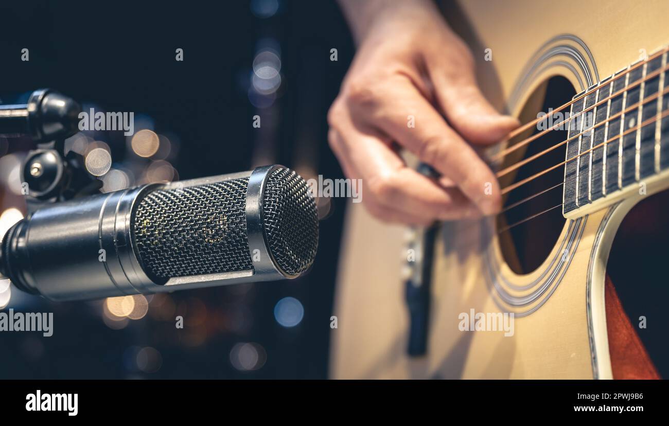 Male musician playing acoustic guitar behind microphone in recording ...