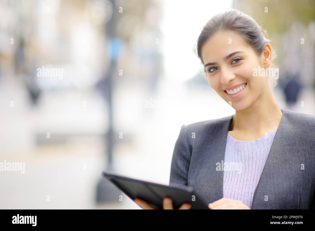 Happy executive posing looking at camera holding tablet outside in the ...