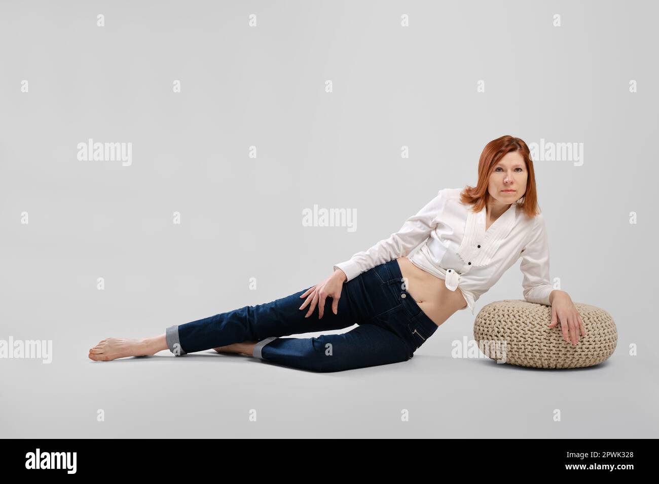 Barefoot middle age woman leaning on padded stool. Studio concept of ...