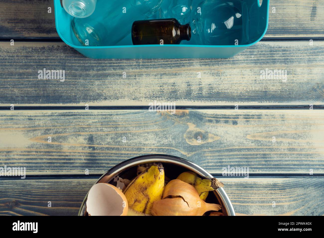 Two halves of plastic and metal containers with organic and plastic waste, rubbish on wooden ...