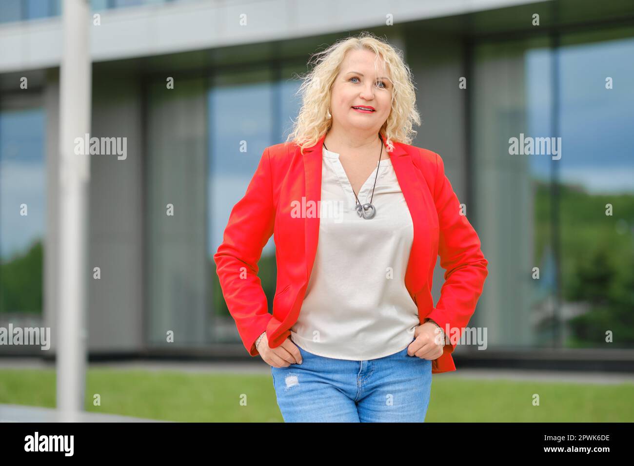 Confident senior woman in red jacket, blouse and denim jeans standing ...