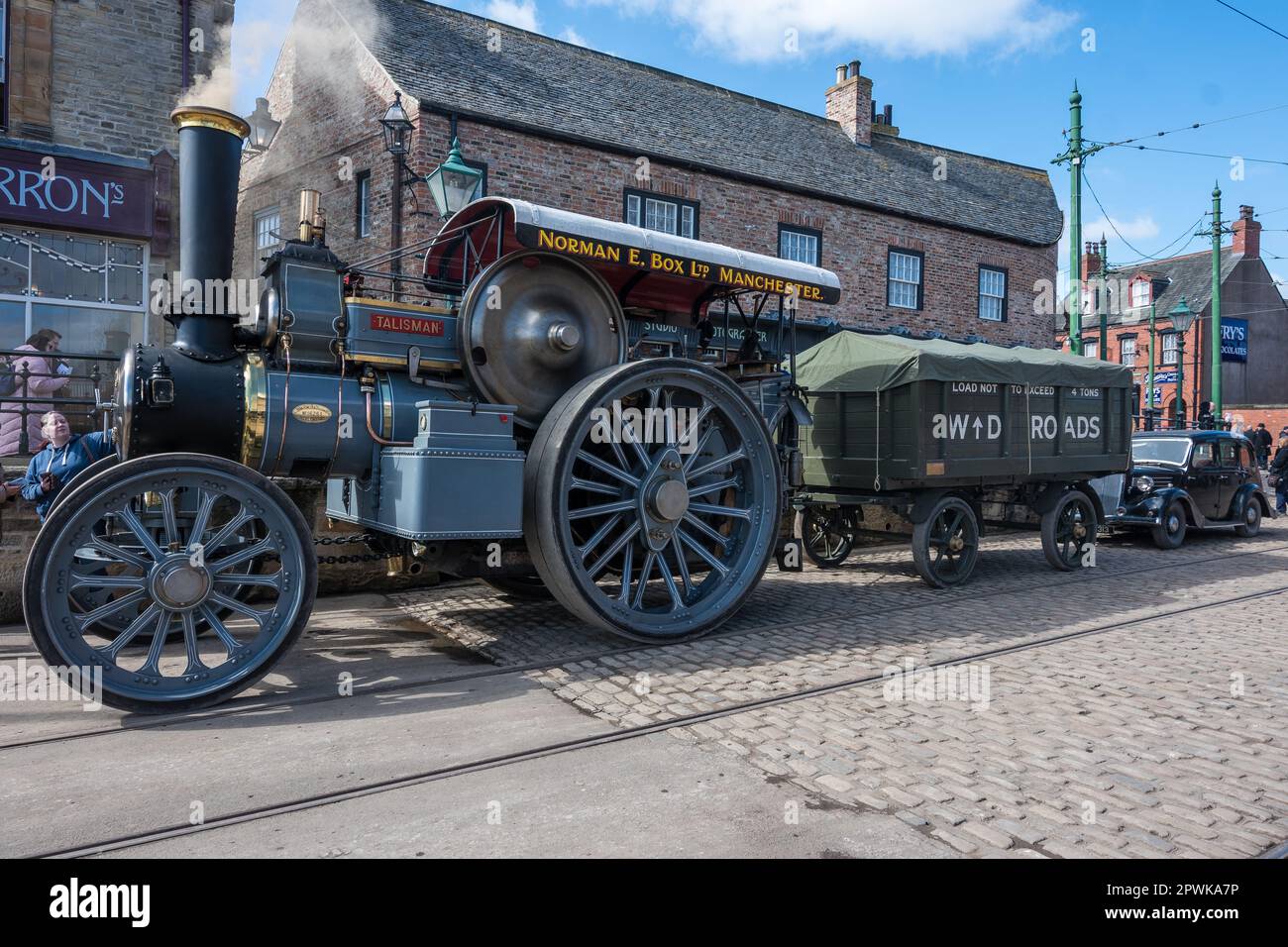 A beautifully restored steam traction engine pulling a trailer along a ...