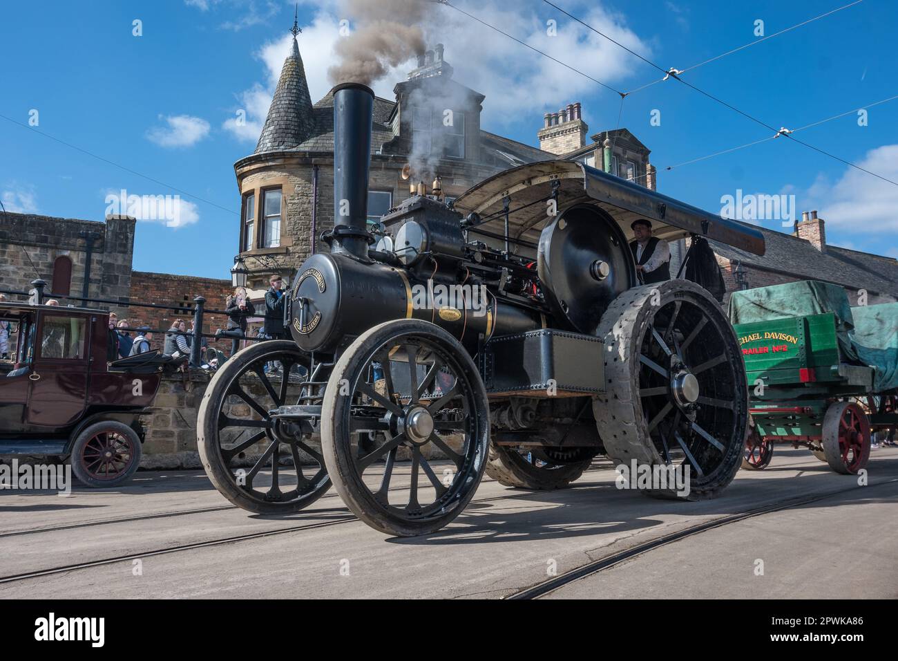 A beautifully restored steam traction engine pulling a trailer along a ...