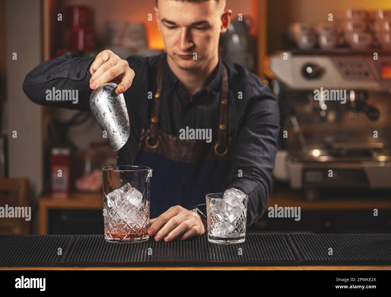 Barman holds metal scoop with ice cubes in his hand and pours them into ...