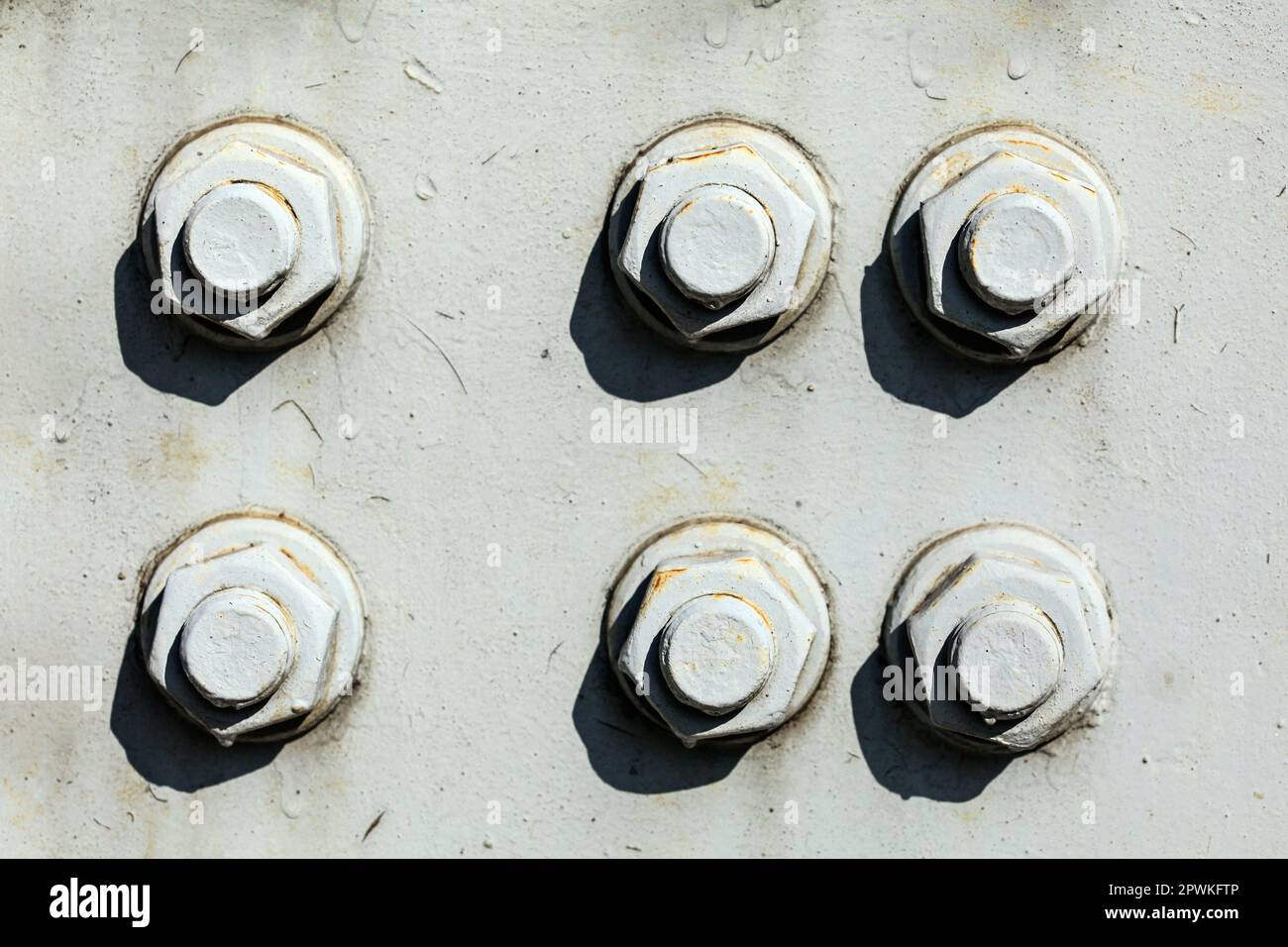 Six large nuts and bolts on gray steel plate of rail bridge, lit by ...