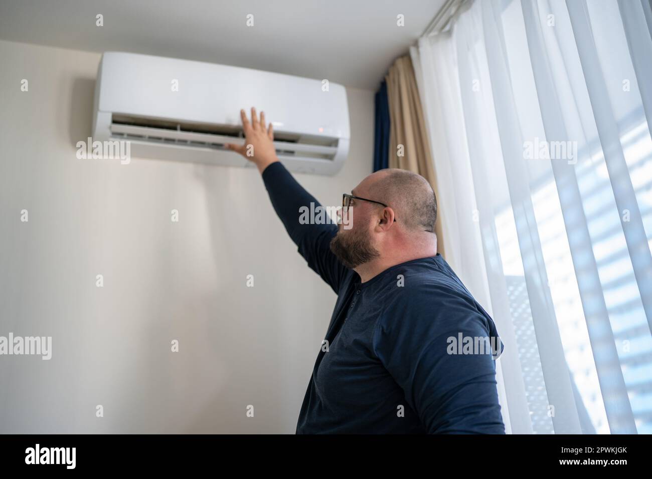 Man checking working air conditioner touching air by hand in summer hot ...