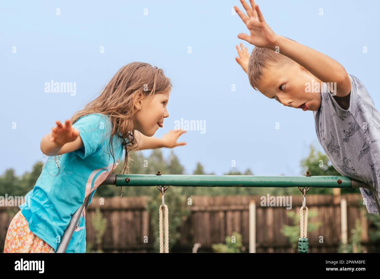Cheerful little girl and boy fool and make faces standing opposite ...