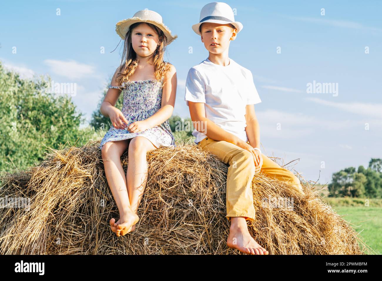 Cute little girl and boy sitting together at top of haystack. Friends ...