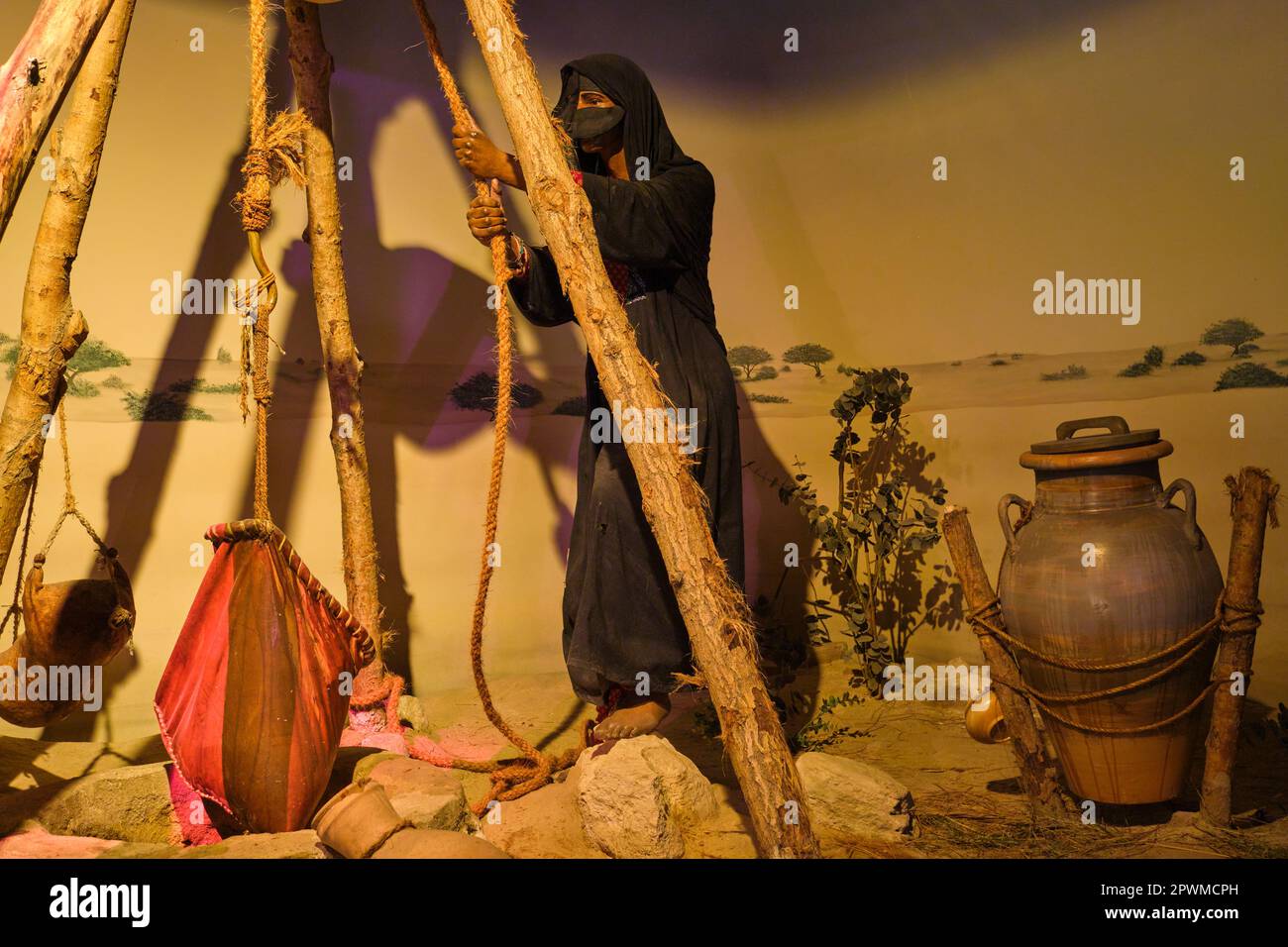 A tribeswoman in a black burka hauling up water from a desert well with ...