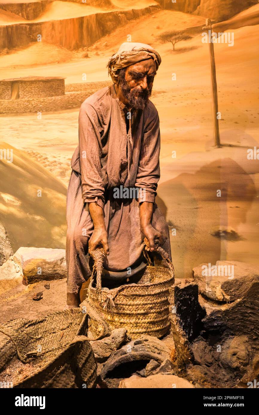 A bearded worker, miner, hauling a heavy basket of rocks. A diorama ...