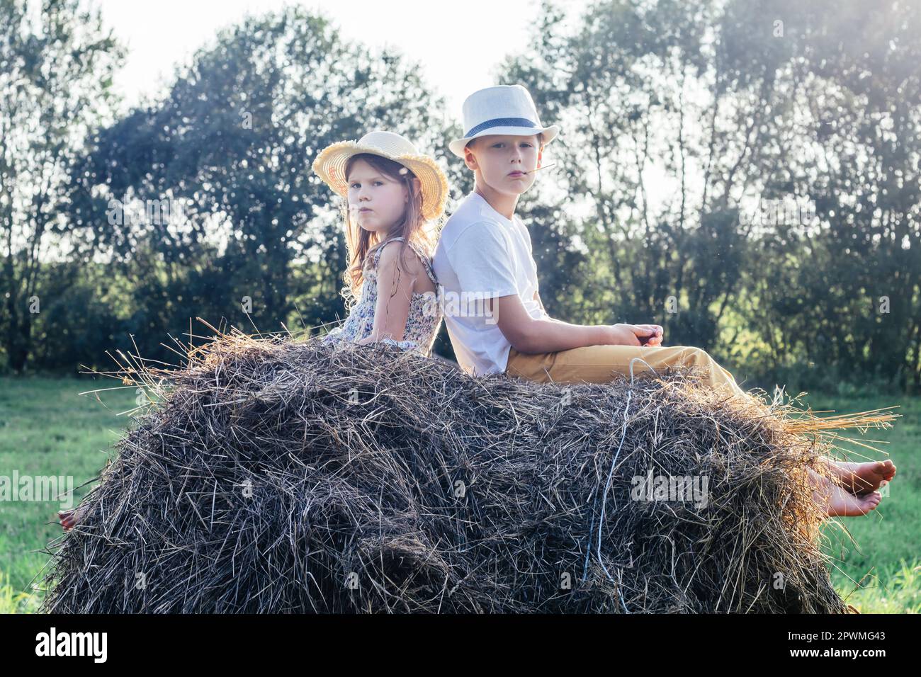 Portrait of two barefoot children boy and girl sitting on haystack in ...