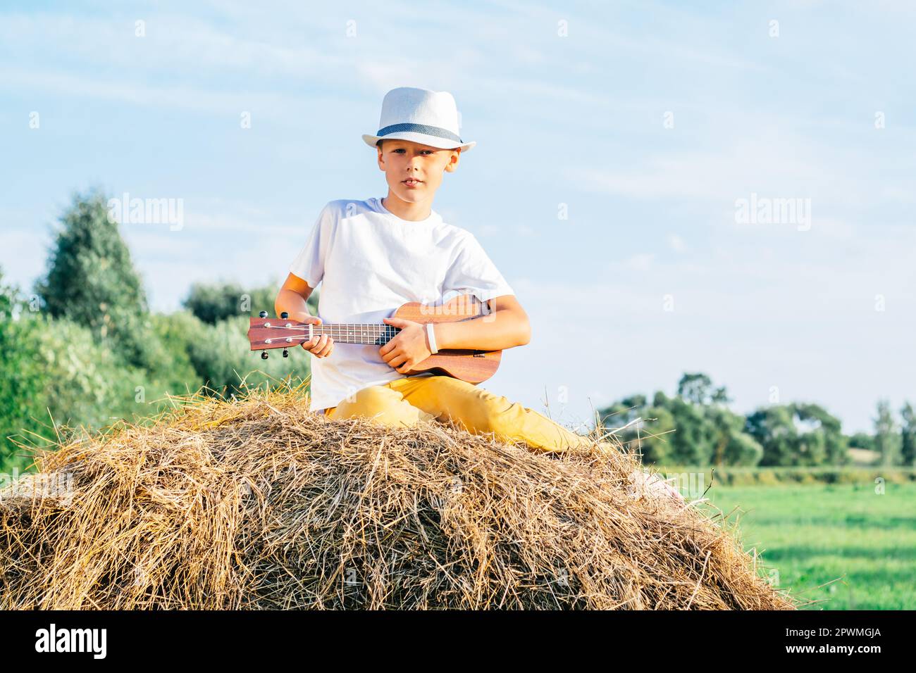 Portrait of barefoot boy in hat on haystack in field. Playing small ...