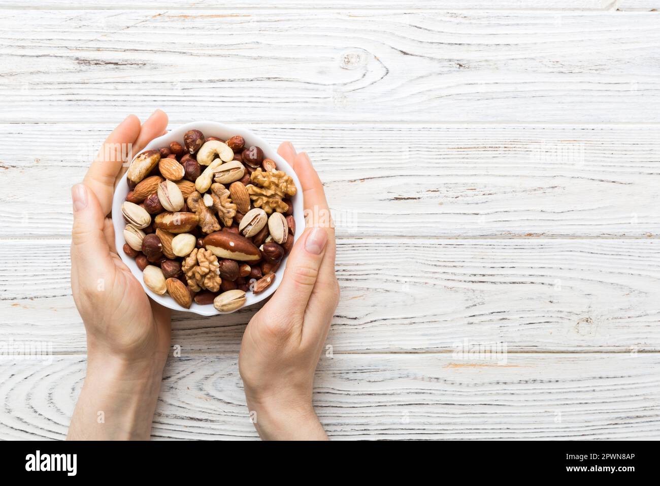 Woman hands holding a wooden bowl with mixed nuts Walnut, pistachios ...