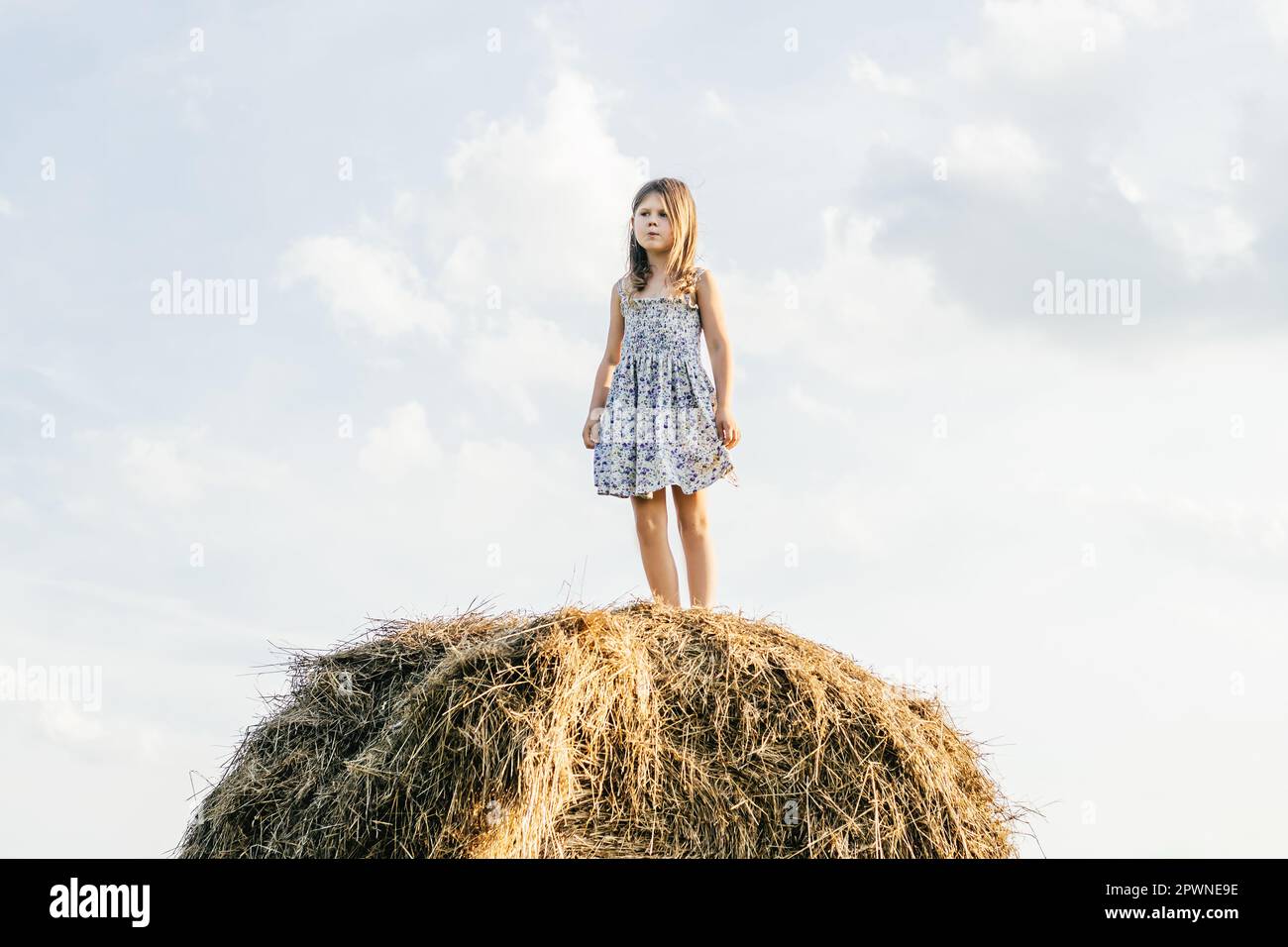Pretty little girl stand at top of haystack looking away. Full length ...