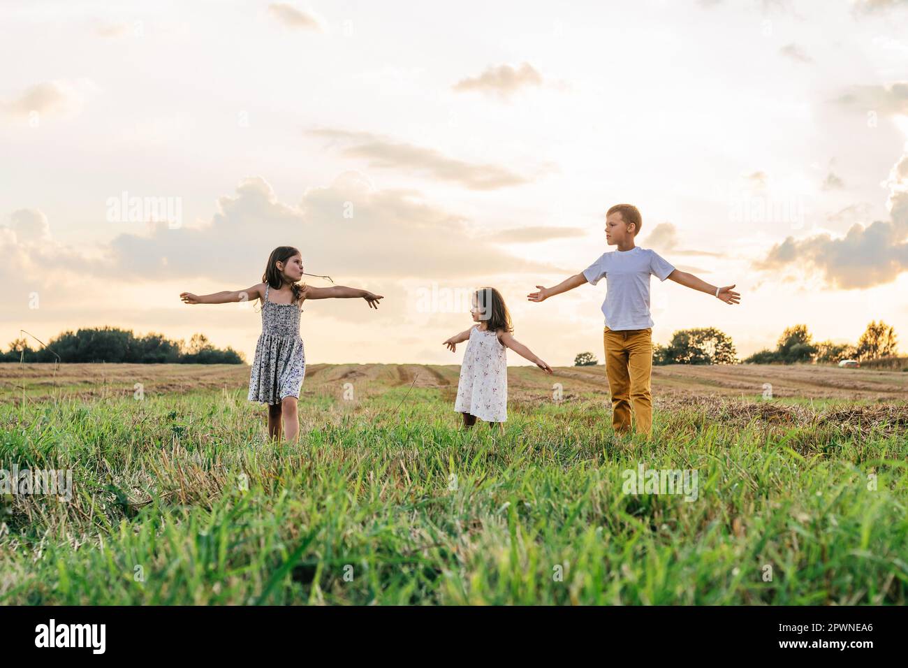 Little children stand together on field and raise arms open wide ...