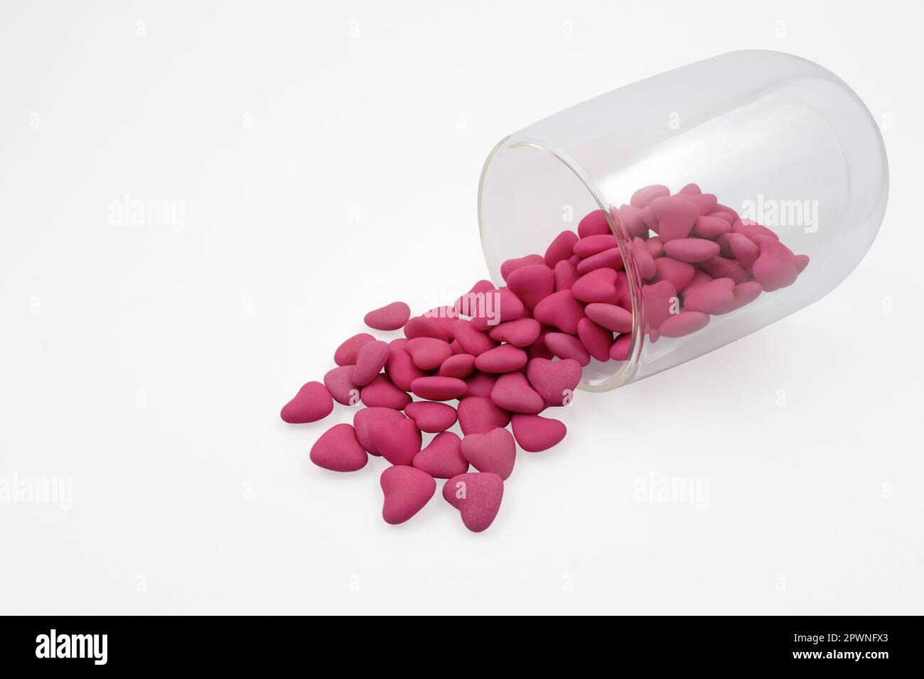 Overturned glass with heart shaped pink candies (close-up) isolated on ...