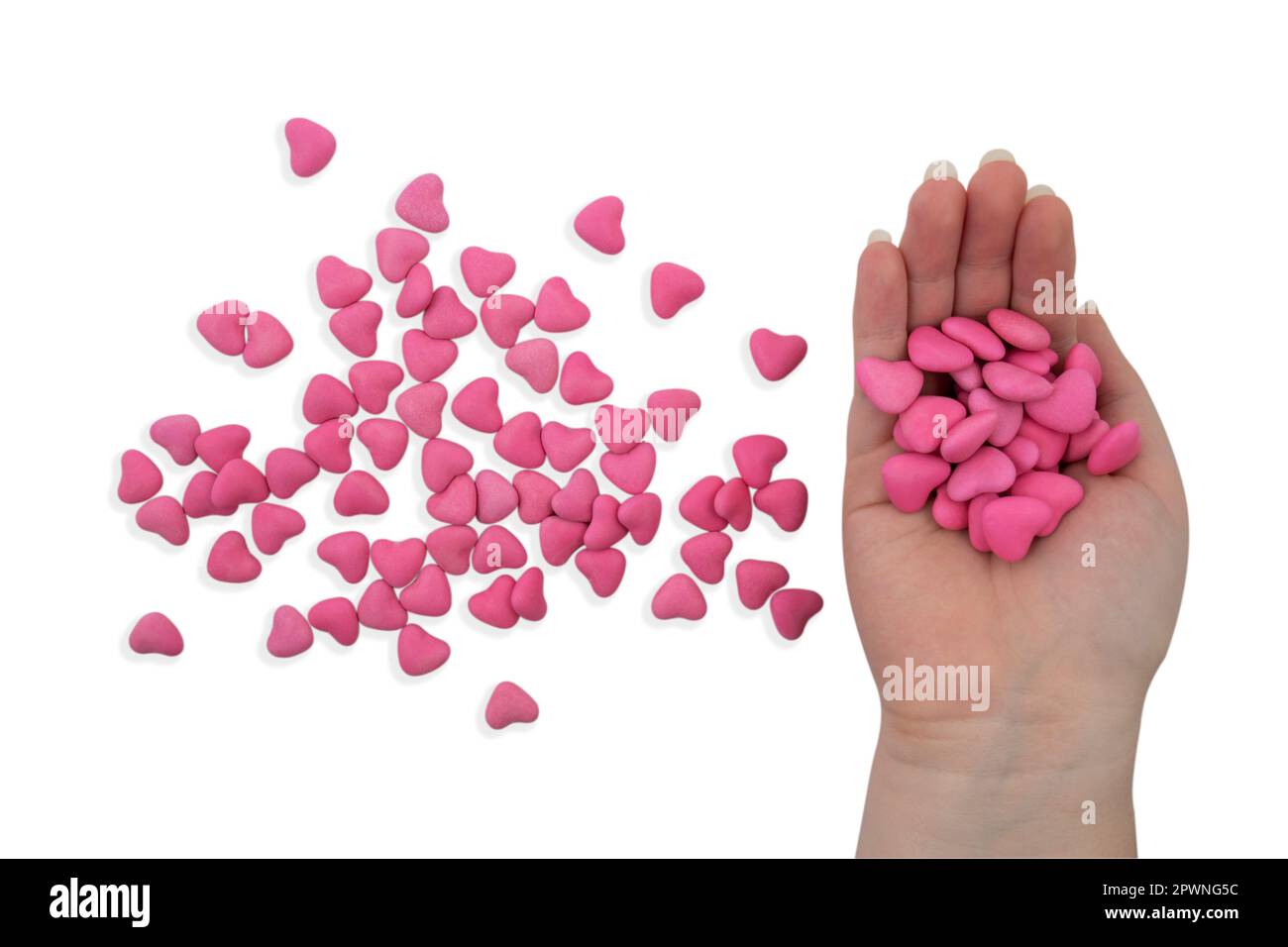 A handful of pink candies in the shape of a heart in a hand isolated on ...