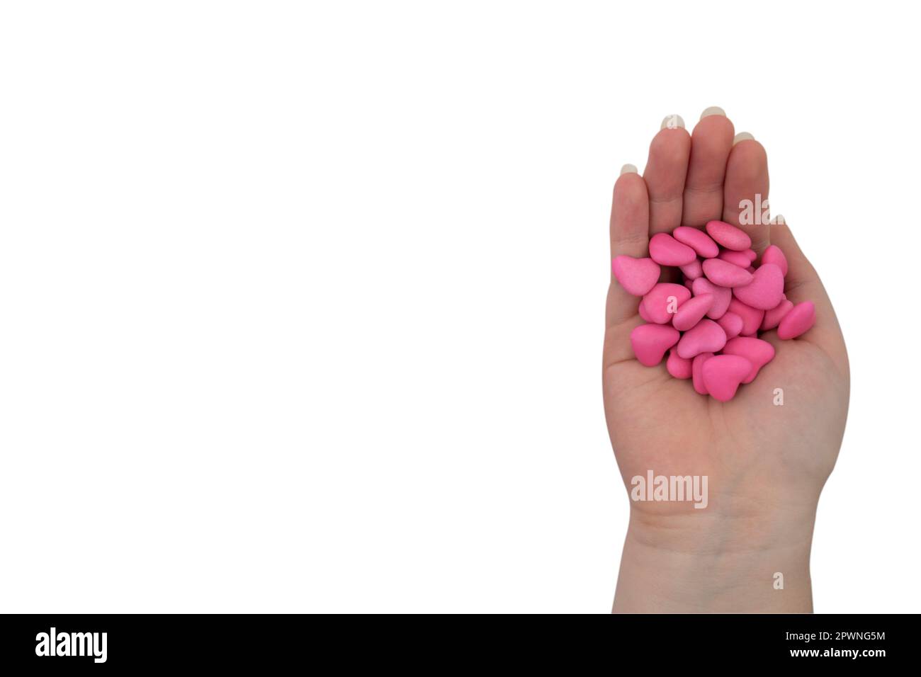 A handful of pink candies in the shape of a heart in a hand isolated on ...